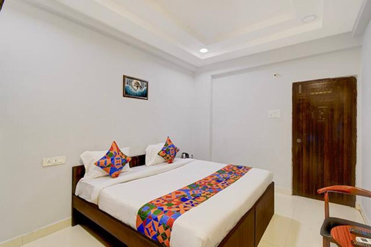 Quarto de hotel com cama, duas almofadas, manta colorida, porta de madeira e uma cadeira pequena.