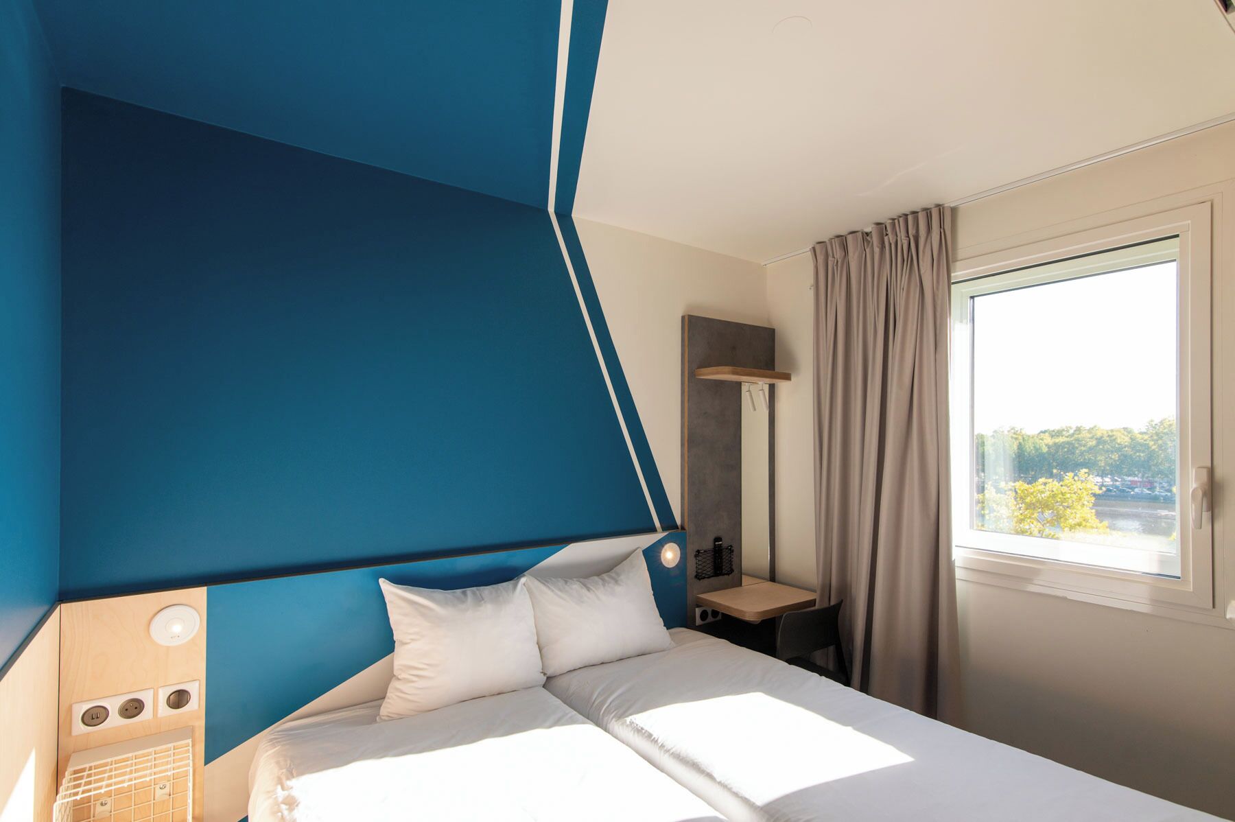 Quarto de hotel com uma cama, uma escrivaninha e uma janela com cortinas.