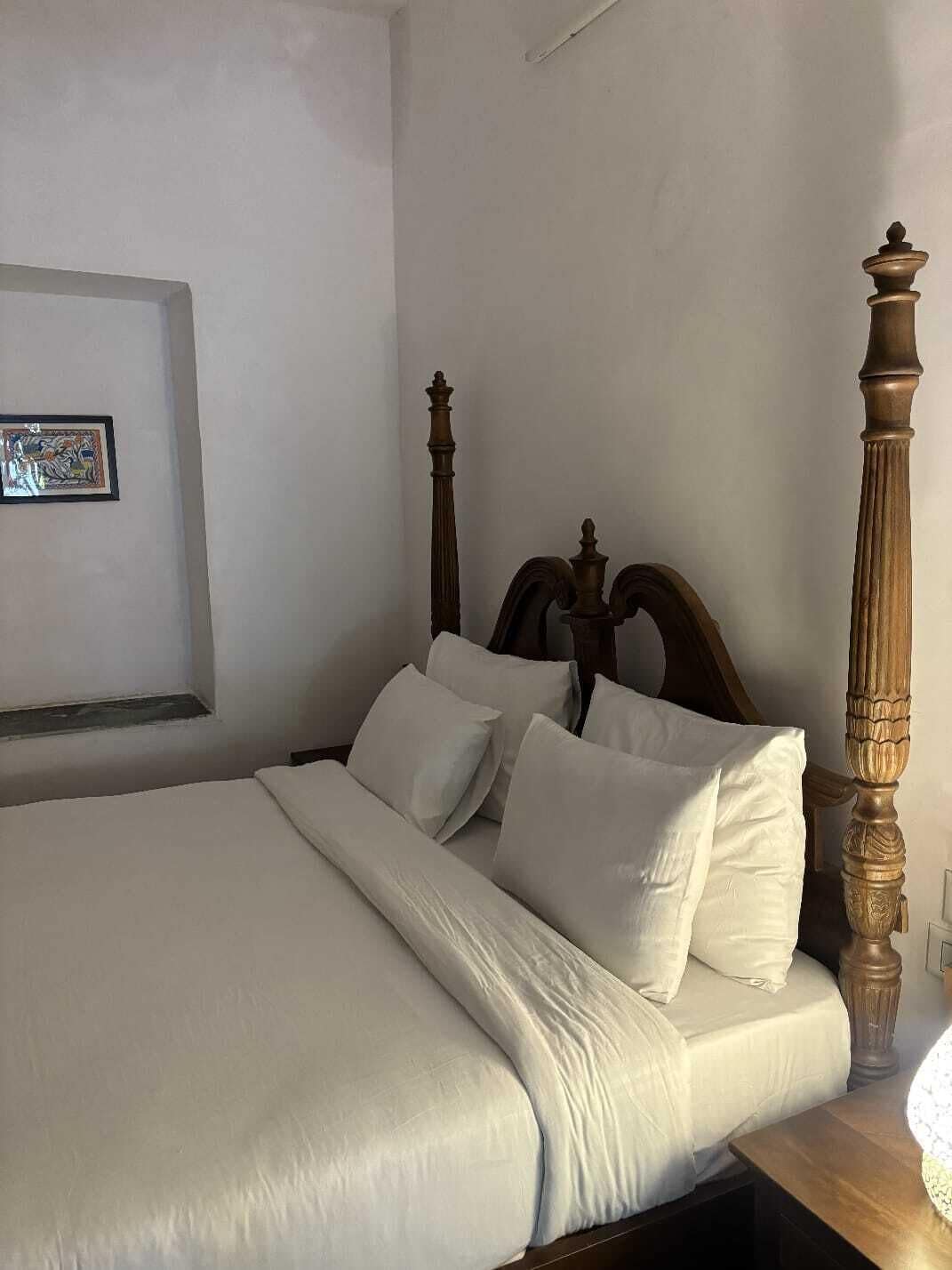 Cama bem arrumada com lençóis brancos, cabeceira de madeira e um quadro na parede.