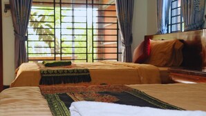 Quarto de hotel com duas camas, uma janela com grades de metal e cortinas.