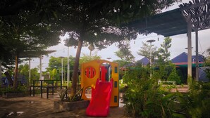 Um parquinho com um escorrega amarelo e um escorrega vermelho, cercado por árvores e plantas.