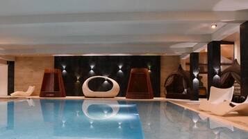 Uma área interna de piscina moderna, com piscina transparente, espreguiçadeiras e arranjos de assentos originais.