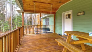 Um deck de madeira com mesa de piquenique e banco, um balanço e uma porta com a placa 'Open'.