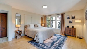 Quarto com cama grande, mesa de cabeceira, abajur, cômoda e janela com cortinas.