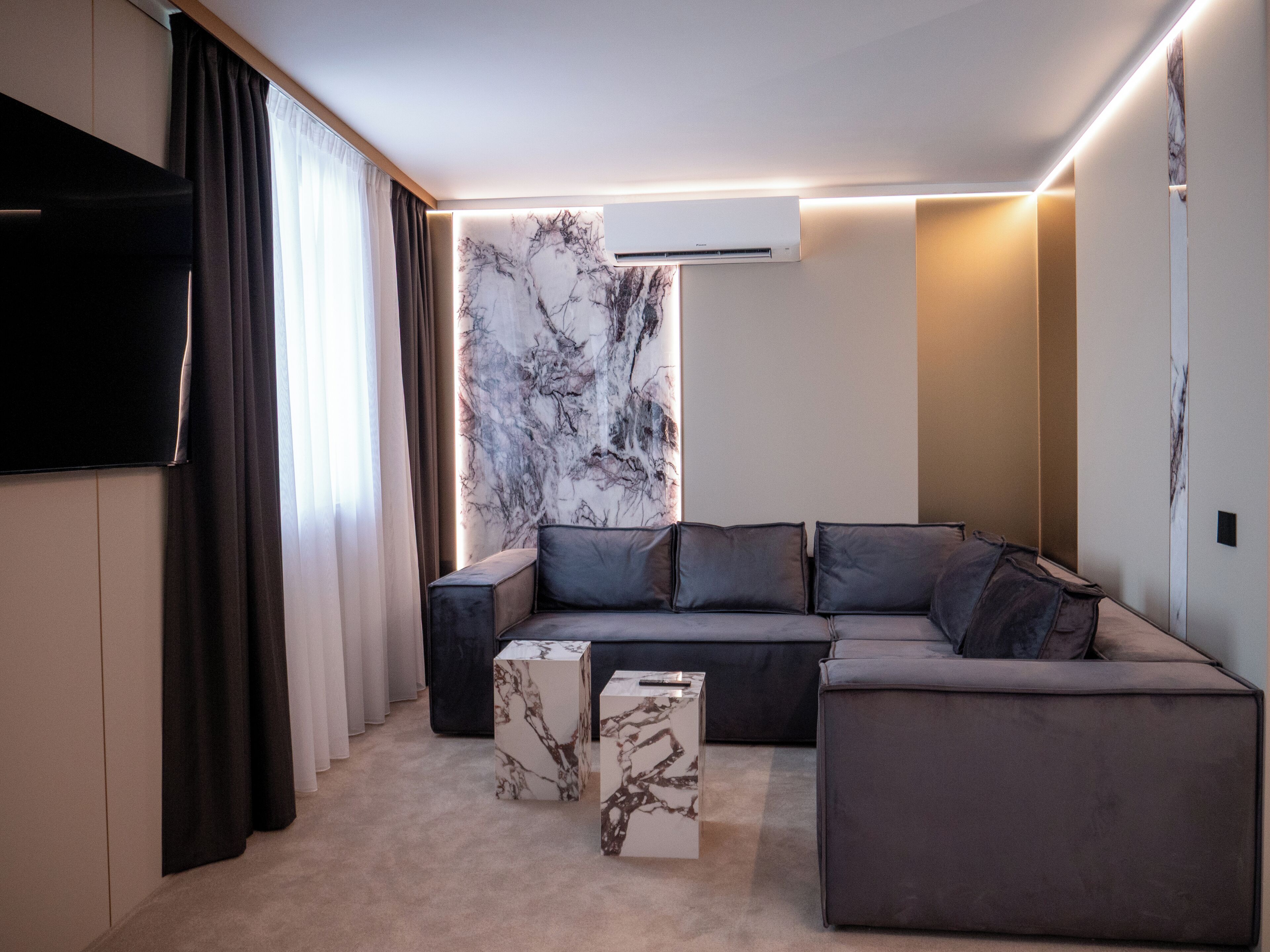Uma sala de estar moderna com sofá seccional, detalhes em mármore e TV de tela plana na parede.