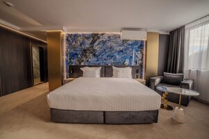 Uma cama grande com cabeceira de mármore, uma mesinha redonda e um sofá num quarto de hotel moderno.