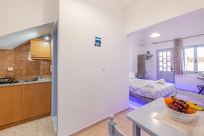Quarto compacto com cozinha compacta, uma cama com colcha branca e uma mesa com uma fruteira.