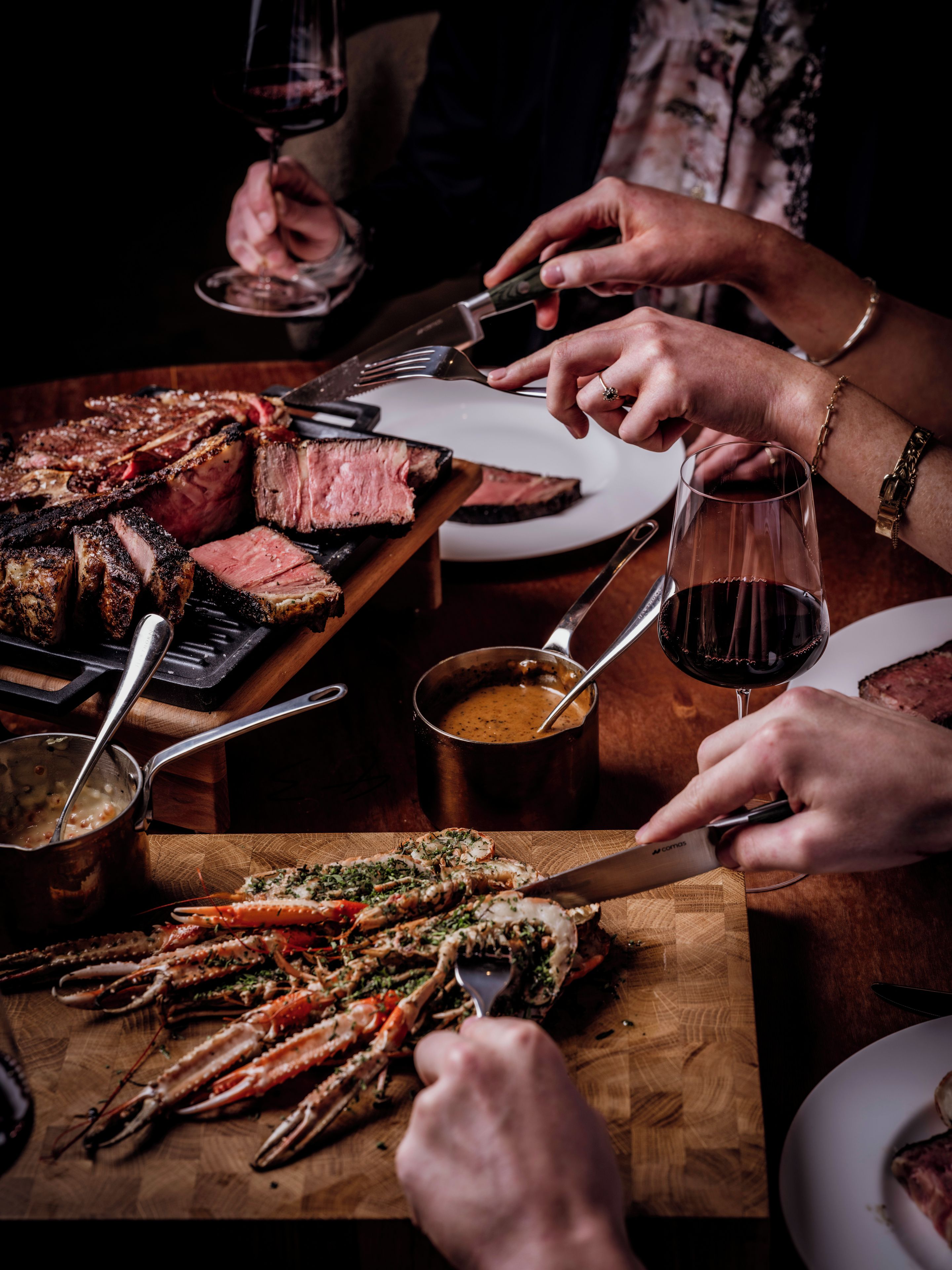 Uma mesa de jantar com diversos pratos, incluindo lagosta, bife e uma tigela de sopa.