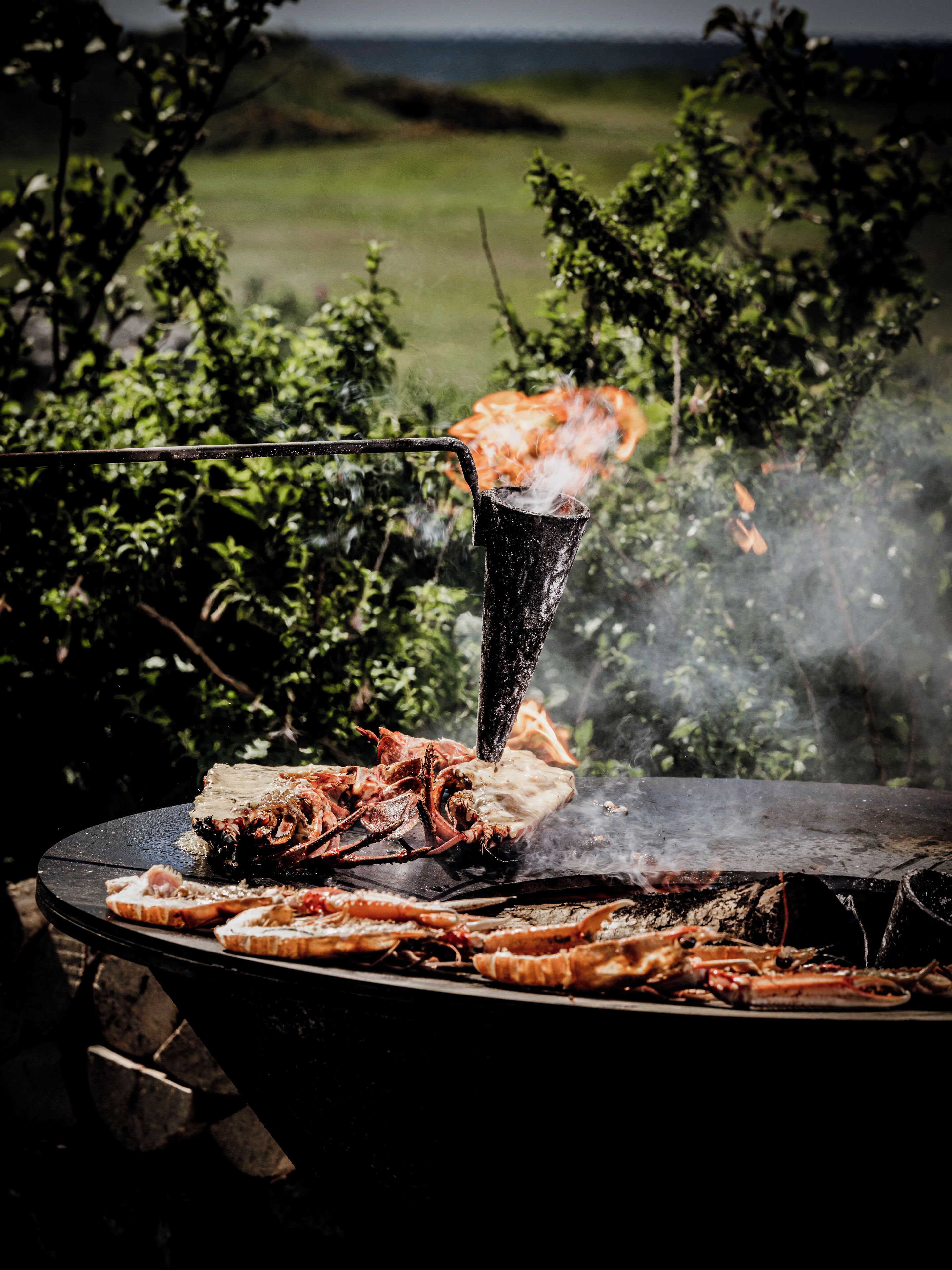 Uma churrasqueira com frutos do mar e carne a ser preparada ao ar livre.
