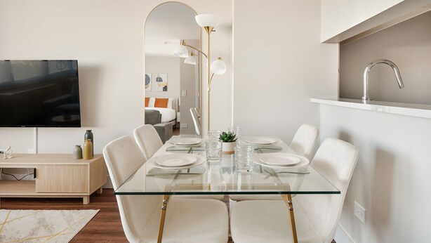 Uma área de refeições moderna com mesa de vidro, cadeiras brancas e decoração minimalista.