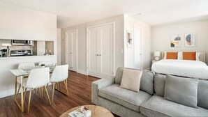 Quarto de hotel moderno com área de refeições, um sofá cinzento e uma cama com roupa de cama branca.