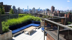 Terraço no telhado com área de estar, guarda-corpo de vidro e vista para o horizonte da cidade.