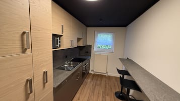 Cozinha moderna com armários de madeira, bancada preta, forno embutido e janela com vista para o verde.