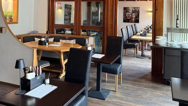Restaurante com vigas de madeira, luminárias pendentes e uma mistura de mesas e cadeiras de madeira e estofadas.