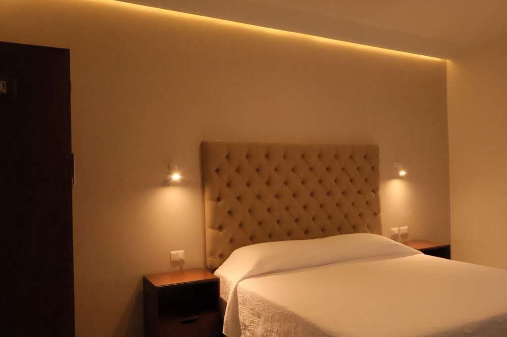 Quarto de hotel com cabeceira estofada, cama com roupa de cama branca e duas mesas de cabeceira com abajures.