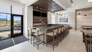 Cozinha moderna com uma ilha grande, banquetas, luminárias pendentes e vista através da porta de vidro.