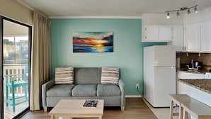 Uma sala de estar com um sofá cinza, uma mesa de centro de madeira e uma pintura de um pôr do sol.
