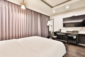 Quarto de hotel moderno com uma cama grande, uma escrivaninha, uma cadeira e uma televisão de tela plana.