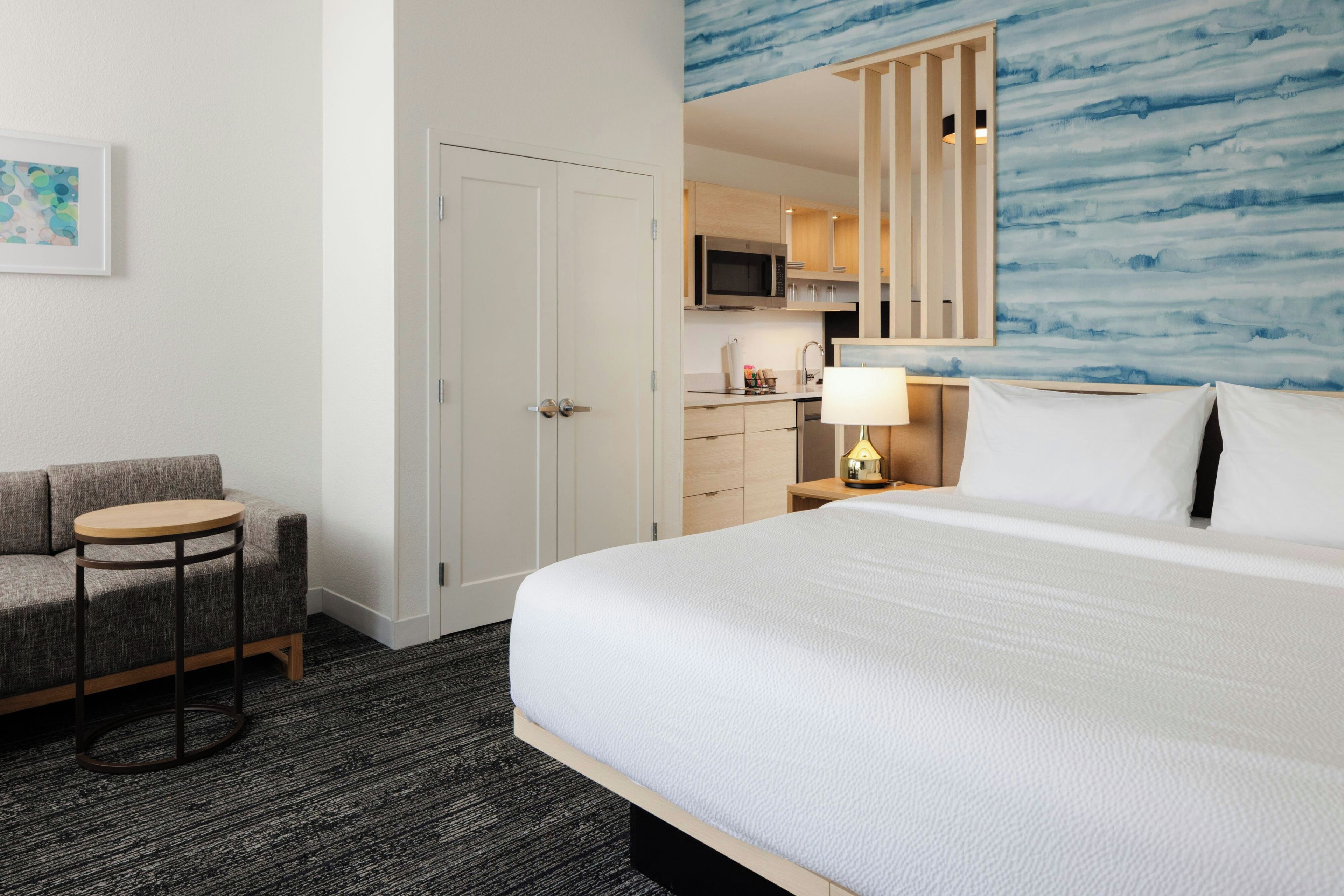 Quarto de hotel com cama, área de estar, cozinha compacta e banheiro.