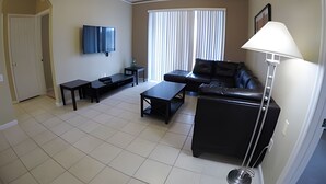 Sala de estar com sofá, mesa de centro, televisão e abajur.