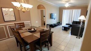 Uma sala de jantar com mesa e cadeiras de madeira, um candelabro e um quadro na parede.