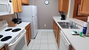 Uma cozinha compacta com eletrodomésticos brancos, armários de madeira e piso ladrilhado.