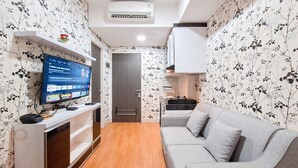 Uma sala de estar moderna com televisão de tela plana, sofá cinza, piso de madeira e papel de parede floral.
