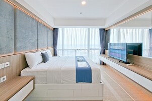 Quarto de hotel moderno com uma cama grande, televisão de tela plana e vista da cidade através de amplas janelas.