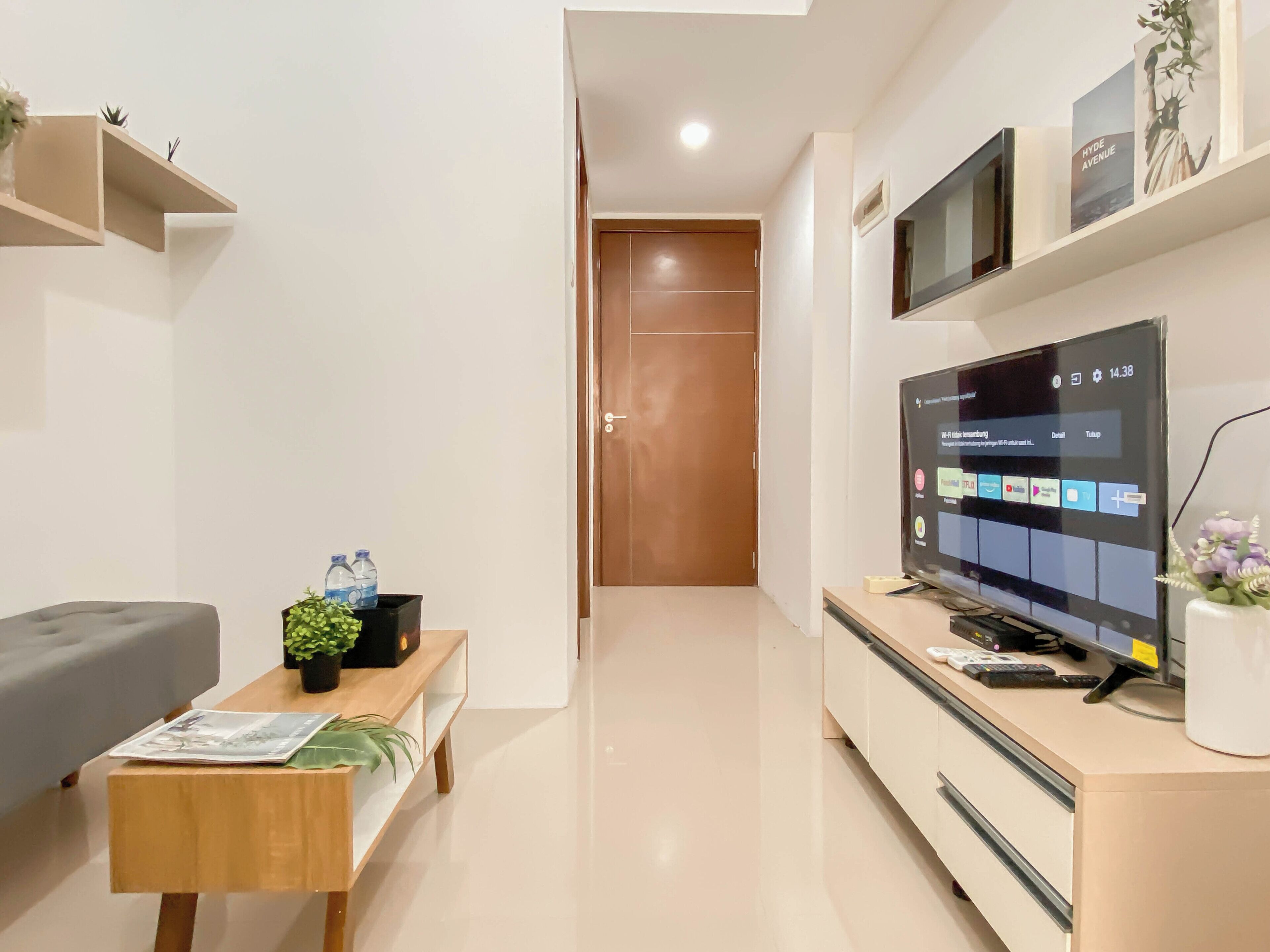 Uma sala de estar moderna com uma televisão de tela plana, um sofá, uma mesa de centro com uma revista e uma pequena planta.