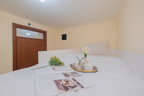 Cama bem arrumada com lençóis brancos, um tabuleiro com objetos decorativos e um pequeno vaso de planta.