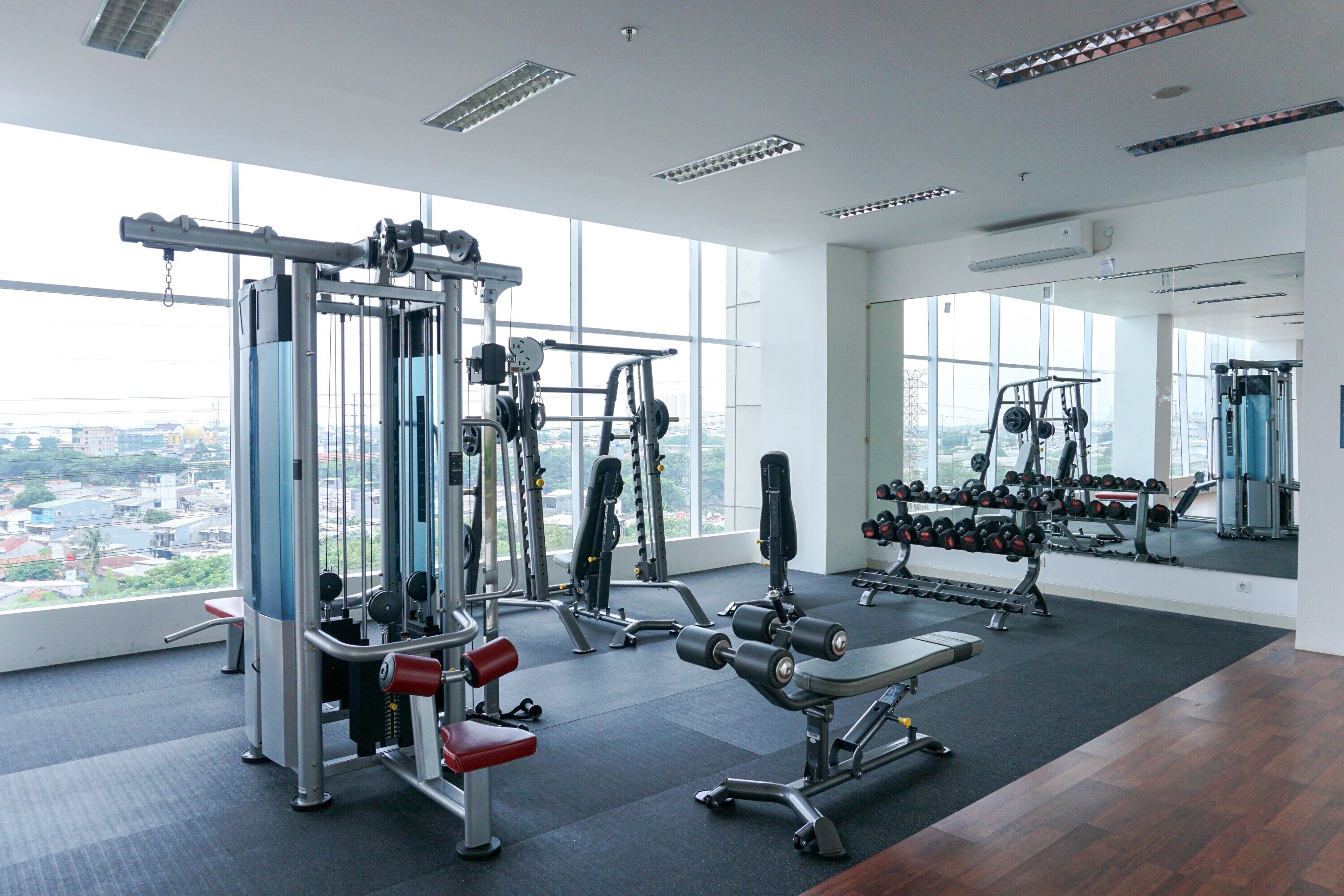 Uma academia com diversos equipamentos de exercícios, amplas janelas e vista para a cidade.