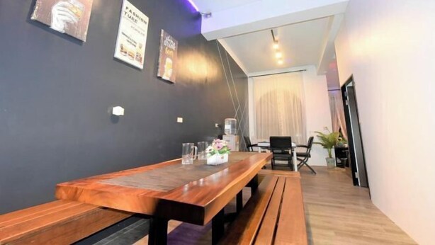 Uma sala de reuniões moderna com uma longa mesa de madeira, paredes pretas e iluminação ambiente roxa.