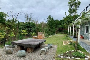 Um jardim com mesa de pedra e assentos, cercado por cascalho e plantas.