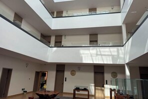 Interior com vários níveis, espaço aberto central, guarda-corpos de vidro e um mezanino.