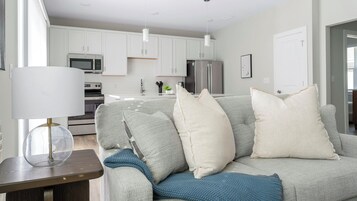 Uma sala de estar moderna com um sofá, uma luminária e uma cozinha ao fundo.