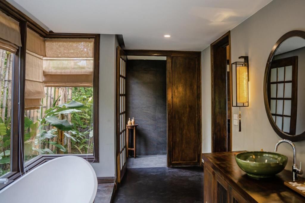 Casa de banho moderna com uma banheira grande, uma bacia verde e vista para um jardim de bambu.