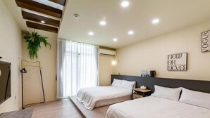 Quarto de hotel com duas camas, uma planta, uma janela com cortinas, uma mesinha de cabeceira e ar-condicionado fixado na parede.