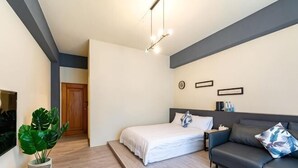 Quarto com cama, sofá, planta em vaso, piso de madeira e luminária no teto.