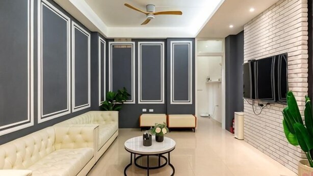 Uma sala de estar moderna com sofá, mesa de centro redonda, ventilador de teto e TV fixada em parede de tijolos.