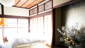 Um quarto japonês tradicional com tatames, uma cama de madeira baixa e uma janela grande com portas de correr.