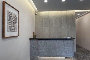 Uma receção com bancada cinzenta, uma obra de arte abstrata emoldurada na parede e um design de interiores moderno.