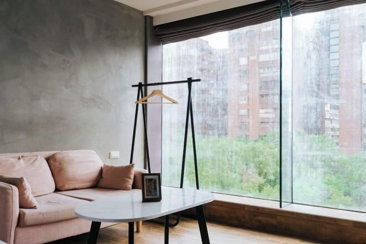 Sala de estar moderna com sofá, mesinha e uma grande janela com vista para edifícios altos.