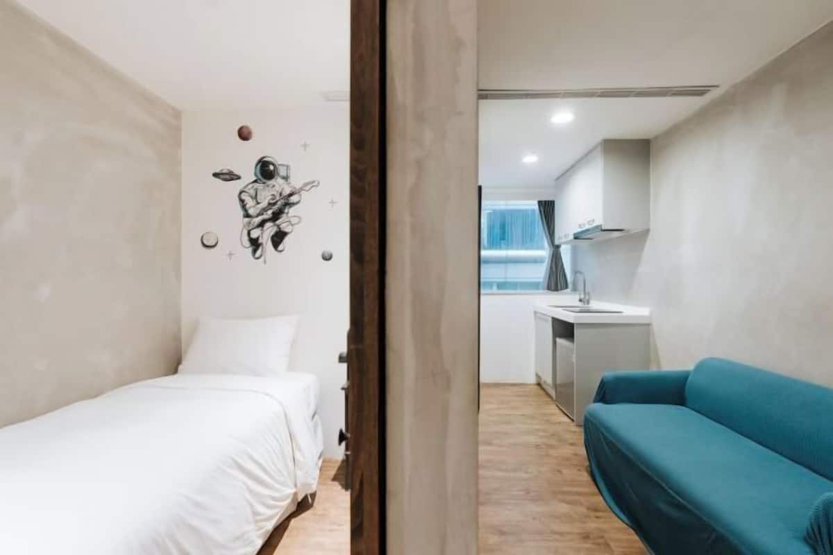 Quarto com cama, sofá azul, cozinha compacta e parede decorada com adesivo de tema espacial.