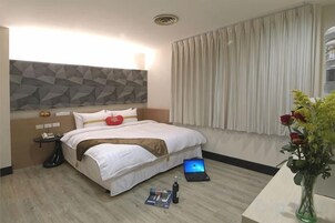 Quarto de hotel com cama, mesa de cabeceira, abajur e um laptop no chão.