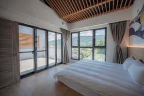 Quarto com cama grande, portas de correr de vidro para uma varanda e vista para o verde.