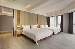Quarto de hotel moderno com duas camas, piso de madeira e uma janela grande com cortinas.