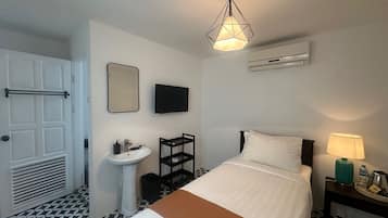 Quarto de hotel com cama, mesa de cabeceira com luminária, televisão, espelho, pia e aparelho de ar condicionado.