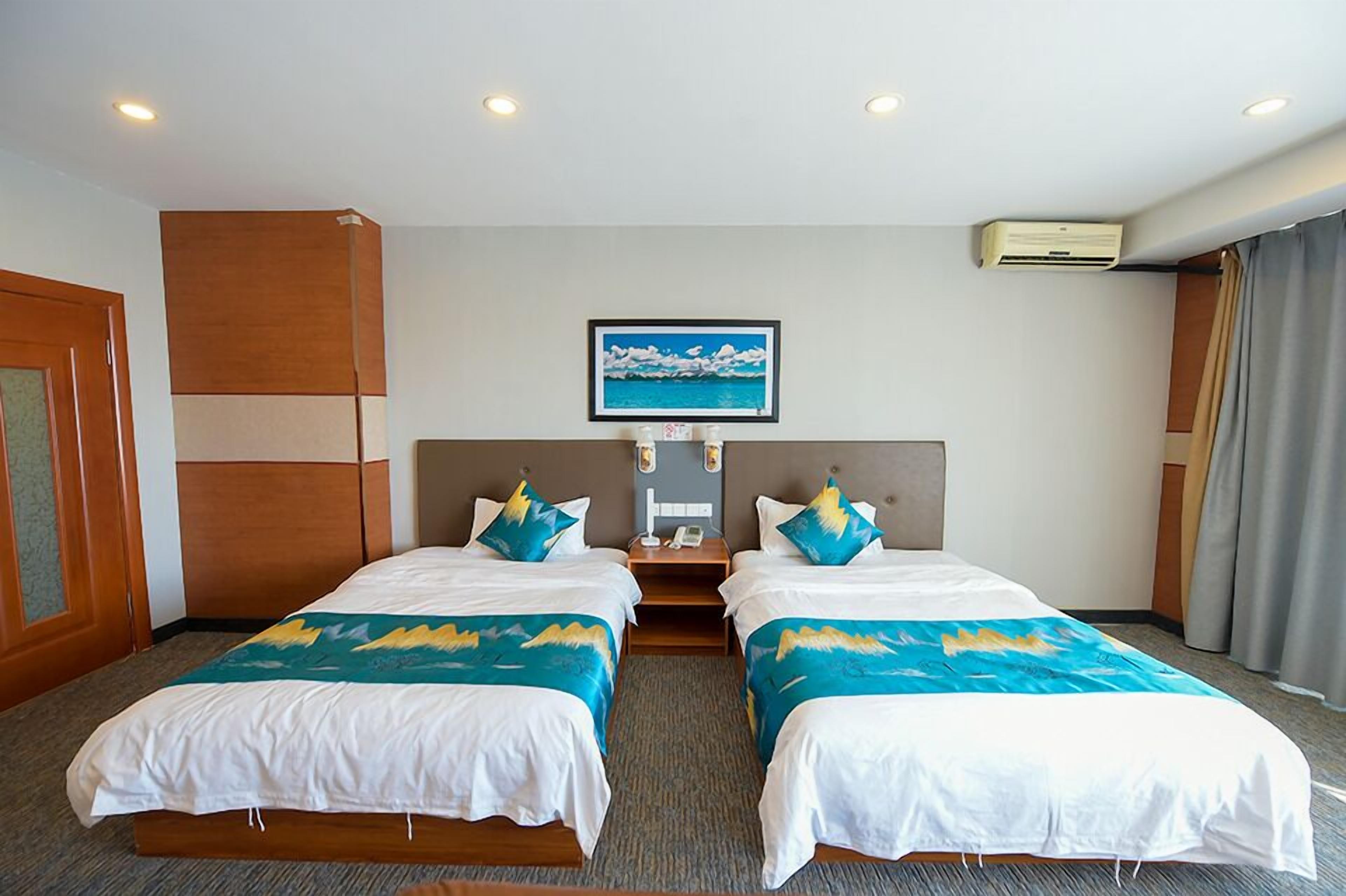 Quarto de hotel com duas camas, um quadro na parede, aparelho de ar condicionado e uma porta.