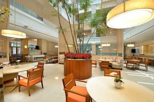 Um amplo saguão de hotel com diversas áreas de refeições, um vaso central com flores e um teto alto com luz natural.
