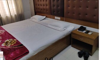Cama bem arrumada com lençóis brancos e um manta floral vermelha, mesa de cabeceira de madeira com um telefone e um abajur, e uma cabeceira estofada marrom.